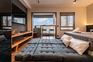 Quarto moderno com uma cama grande, um sofá, uma TV e uma varanda com vista para a cidade.