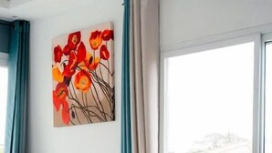 Uma sala de estar moderna com um sofá preto, um quadro de flores vermelhas e uma vista através de uma grande janela.