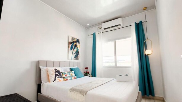 Quarto moderno com cama, mesa de cabeceira, janela com cortinas e ar condicionado.