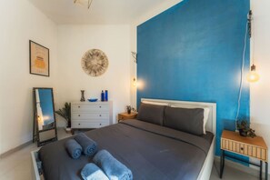 Quarto com cama, penteadeira, espelho e parede com detalhes em azul.