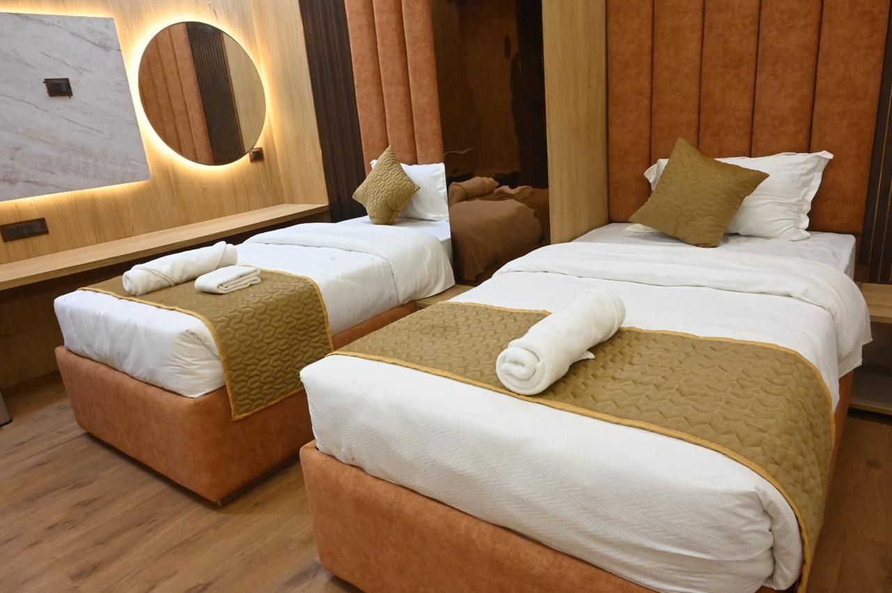 Quarto de hotel com duas camas, um espelho grande e piso de madeira.