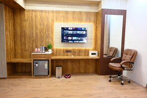 Um espaço de escritório moderno com escrivaninha de madeira, monitor de computador, cadeira e um frigorífico pequeno.