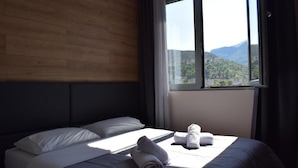 Quarto de hotel com cama, janela vista para montanhas e cabeceira de madeira.