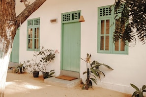 Um edifício com persianas verdes, uma porta e plantas em vasos.