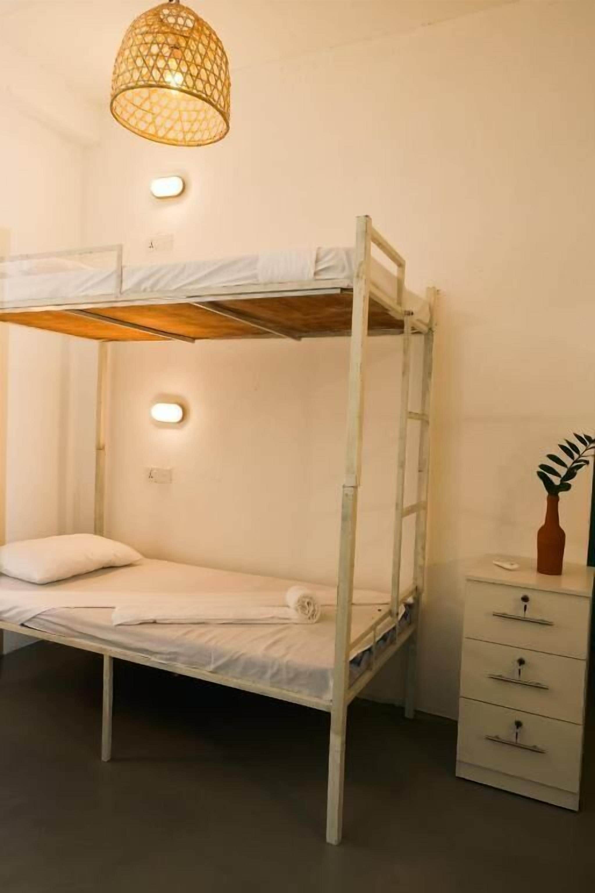 Uma cama beliche com escada, uma mesa de cabeceira com gavetas, uma luminária na parede e um lustre.