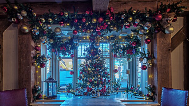 Uma sala de jantar com mesa e cadeiras de madeira, uma árvore de Natal e decoração festiva.
