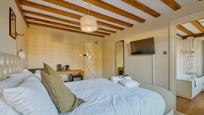 Quarto com cama, mesa de cabeceira, luminária e banheiro com banheira e chuveiro.