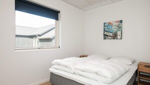 Um quarto com uma cama, uma mesa de cabeceira, uma janela e um cartaz na parede.