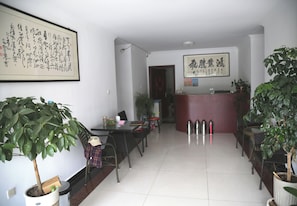 Quarto com uma mesa de recepção, sala de jantar com cadeiras e uma mesa, e plantas em vasos.