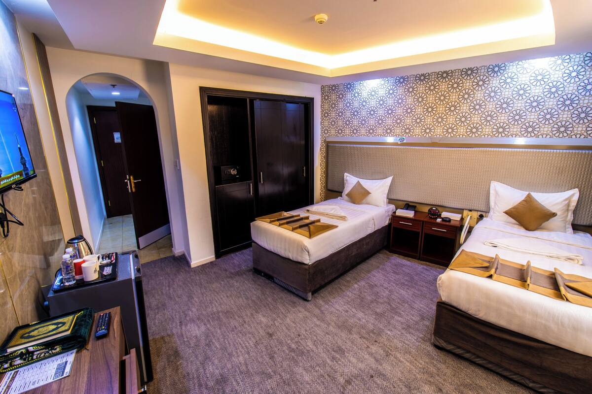 Quarto de hotel com cama, mesas de cabeceira, escrivaninha com computador, televisão e parede estampada.