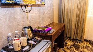 Quarto de hotel com minibar, uma pequena mesa com chaleira, bandeja com garrafas de água, cafeteira e controle remoto.