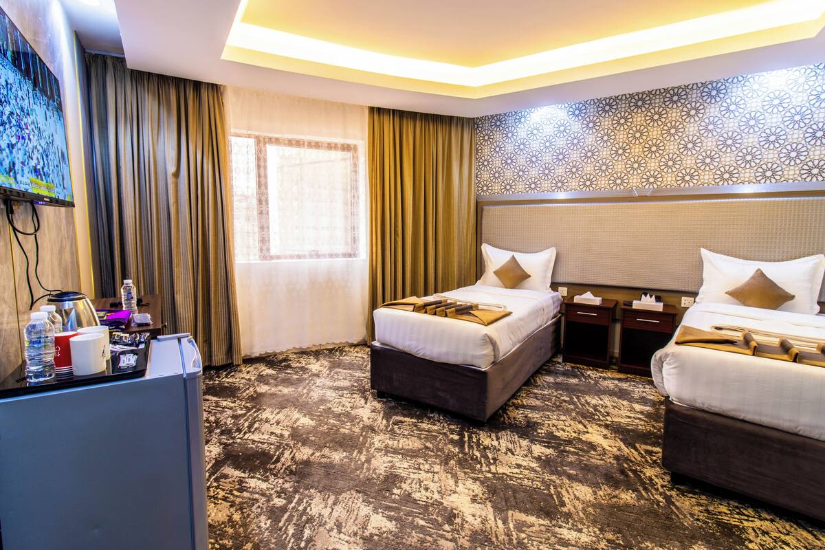 Quarto de hotel com duas camas, televisão, minibar e papel de parede estampado.