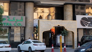 Um edifício com grandes janelas em arco e uma placa com a palavra 'Hotel' em inglês e árabe.