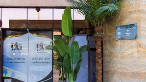 Entrada de hotel com uma grande porta de vidro, placa com o nome do hotel e um código QR.
