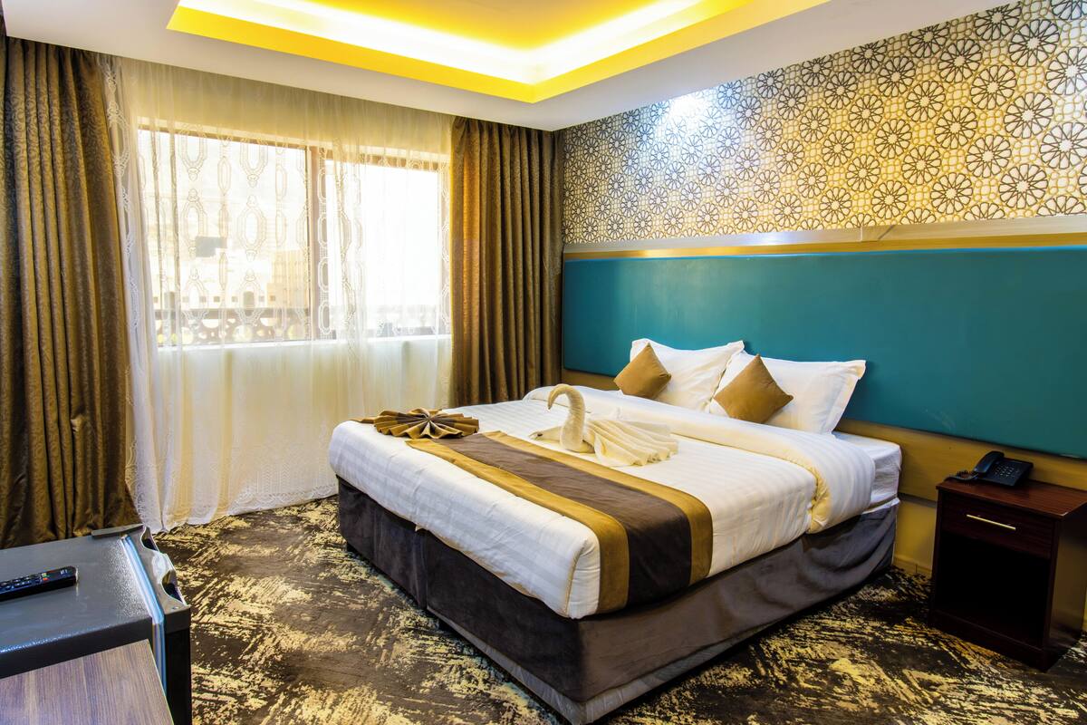 Quarto de hotel com cama, cortinas, parede estampada e mesa de cabeceira.