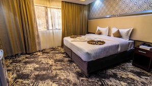 Quarto de hotel com uma cama grande, uma mesa de cabeceira e um papel de parede estampado.