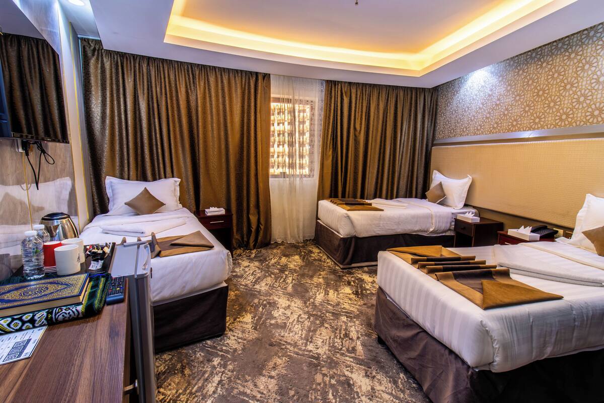 Quarto de hotel com duas camas, uma mesa de escritório com computador, uma cafeteira e uma janela com cortinas.