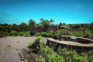 Um jardim com uma estrutura de pedra circular, um caminho de cascalho e diversas plantas.