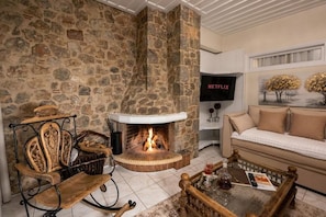 Uma lareira de pedra com uma TV montada acima, um sofá e uma cadeira de balanço de madeira.