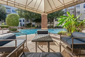 Uma área junto à piscina com espreguiçadeiras, uma mesa e um espaço de estar coberto.