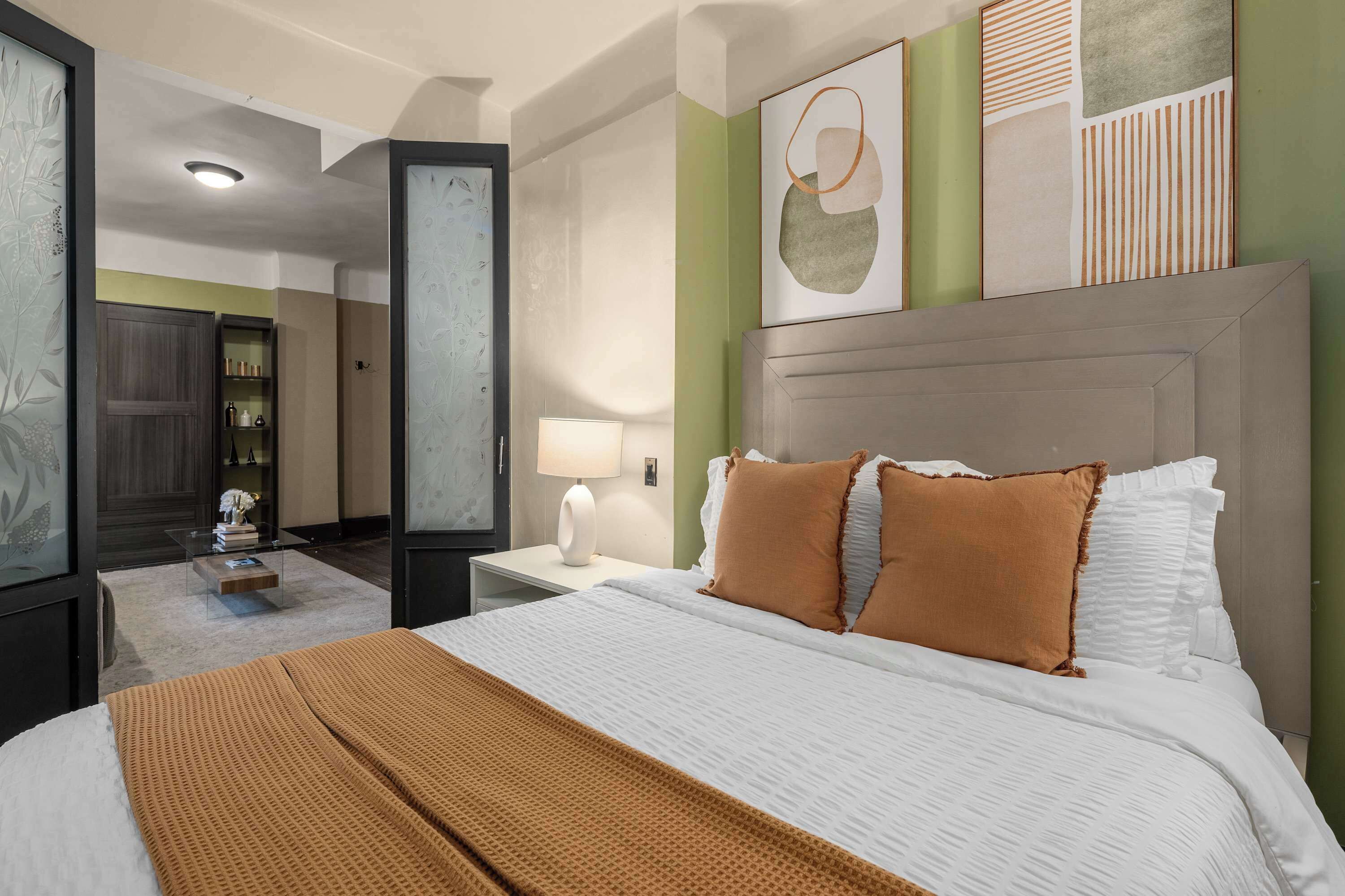 Quarto de hotel com uma cama grande, uma mesa de cabeceira, uma luminária e uma parede com arte abstrata.