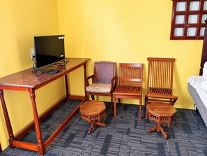 Quarto com escrivaninha, duas cadeiras, um banquinho pequeno, uma cama e uma janela.
