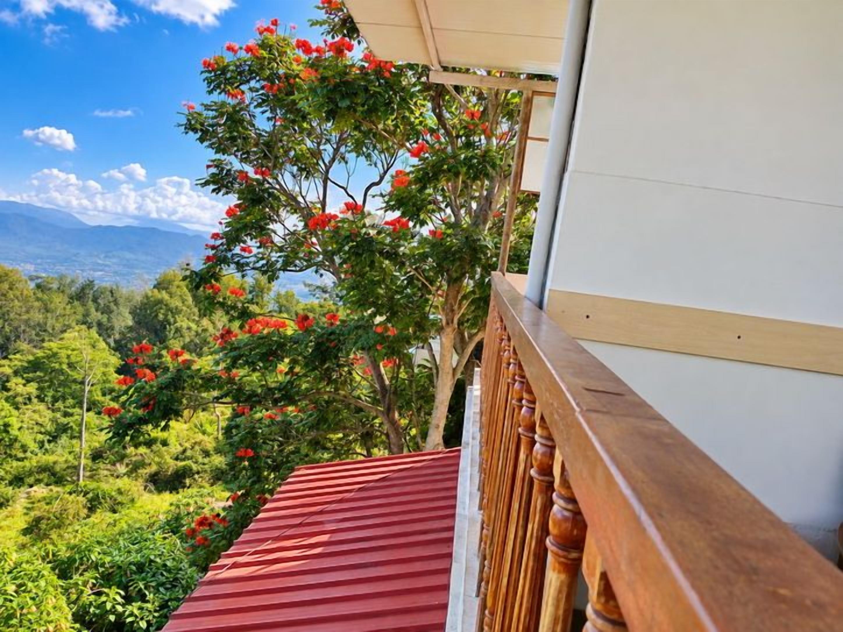 Varanda com telhado vermelho com vista para uma paisagem verdejante e uma cadeia de montanhas.
