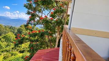 Varanda com telhado vermelho com vista para uma paisagem verdejante e uma cadeia de montanhas.