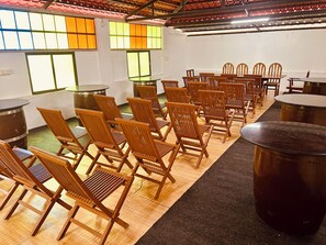 Um espaço com fileiras de cadeiras e mesas de madeira, grandes barris de metal e janelas com vidro esverdeado.