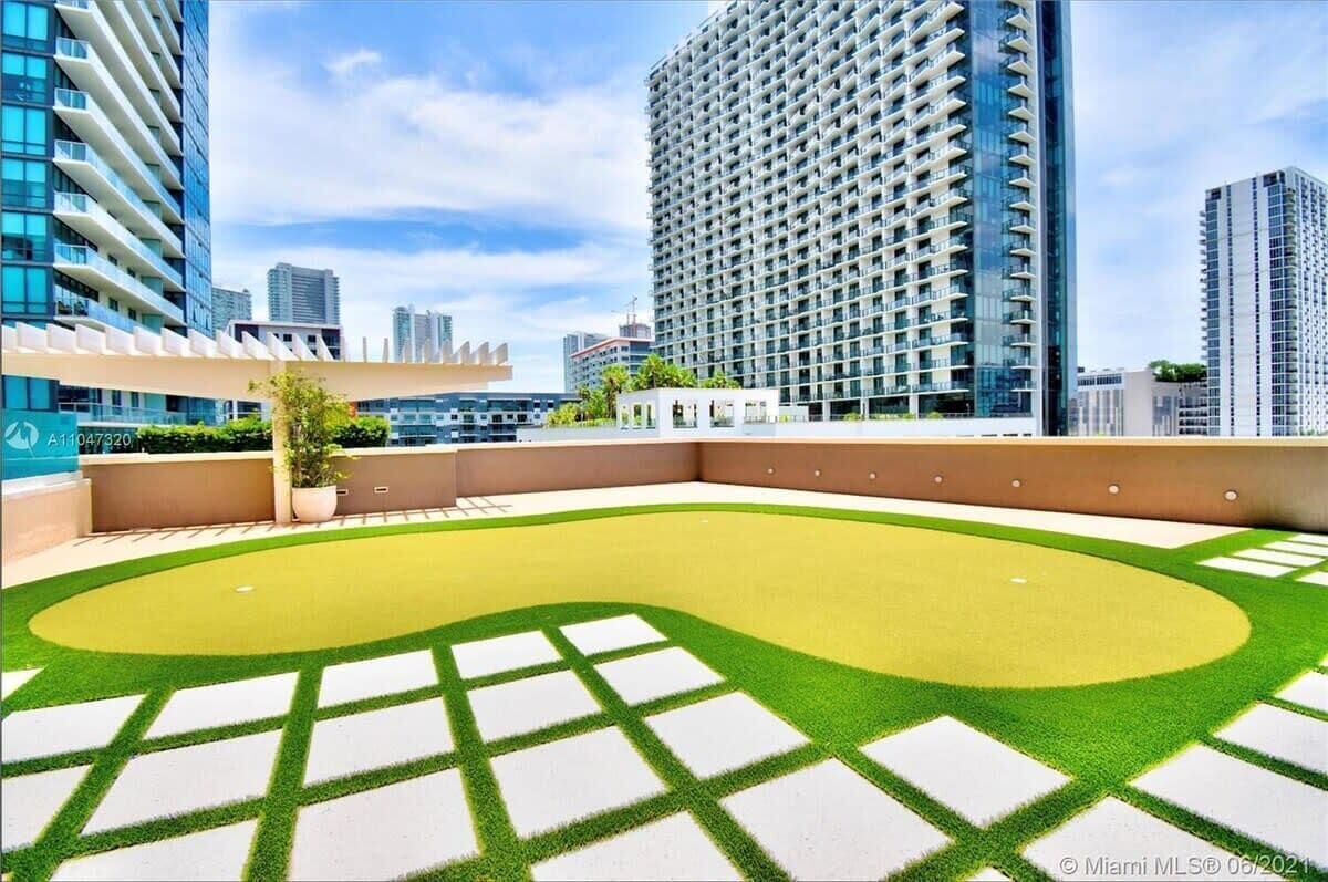Terraço com gramado verde, padrão geométrico branco e edifícios modernos ao fundo.