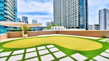 Terraço com gramado verde, padrão geométrico branco e edifícios modernos ao fundo.