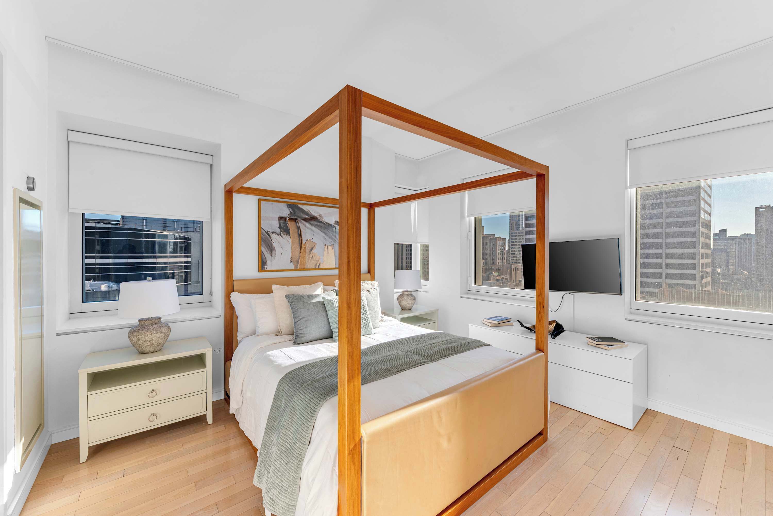 Quarto moderno com cama de dossel, mesa de cabeceira com abajur, criado-mudo e televisão em suporte.