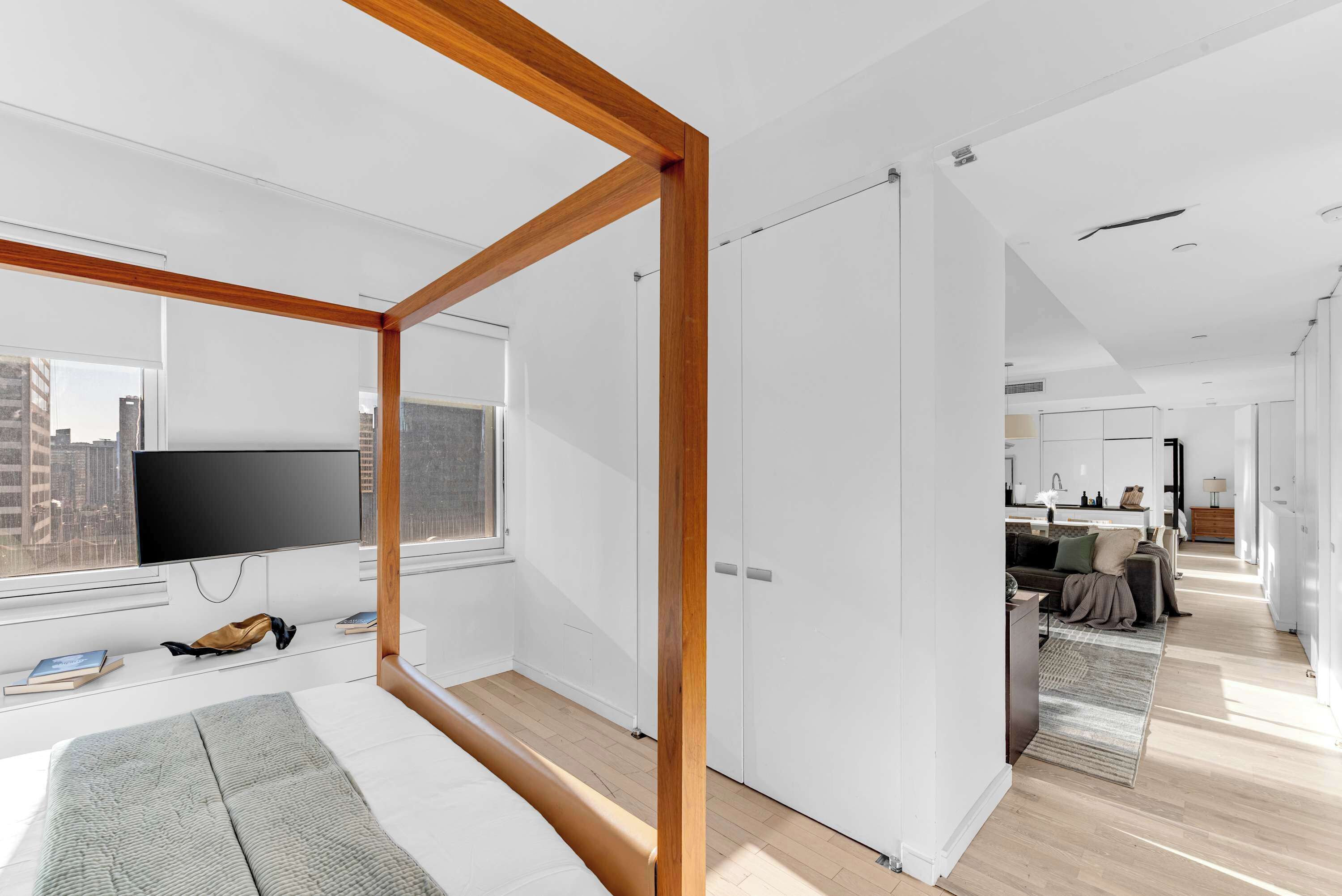 Um quarto moderno e minimalista, com uma janela ampla, uma cama, uma TV e uma porta deslizante que dá para um banheiro.