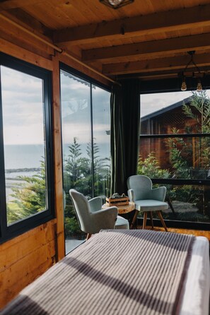 Quarto com uma grande janela, uma cama, duas cadeiras e teto de madeira.