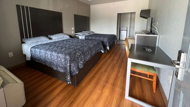 Quarto de hotel moderno com duas camas, uma escrivaninha e uma cozinha compacta.
