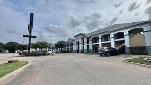 Um hotel com vários andares, pátio central, monumento em forma de cruz e estacionamento com carros.
