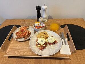 Bandeja de café da manhã com torradas, ovos e um copo de suco de laranja sobre uma mesa de madeira.