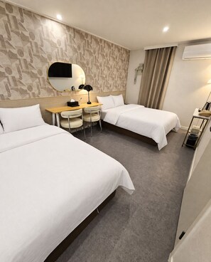 Quarto de hotel com duas camas, uma escrivaninha com cadeiras, um espelho redondo e um aparelho de ar condicionado.