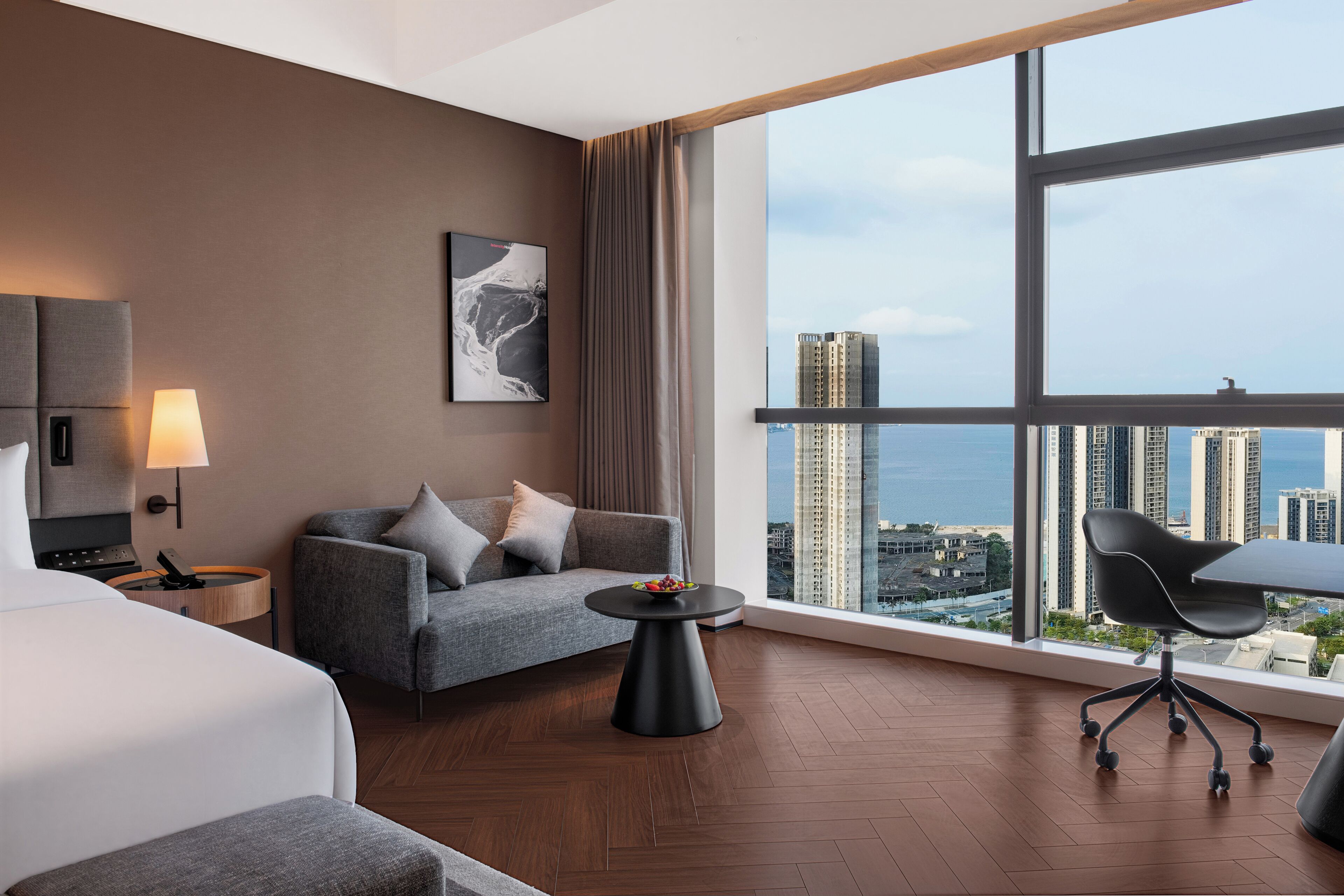Quarto de hotel moderno com uma janela grande, um sofá, uma mesa pequena e uma cama.