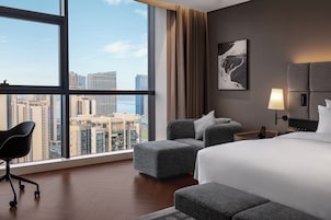 A modern hotel room with a large window, a bed, a desk, and a chair.