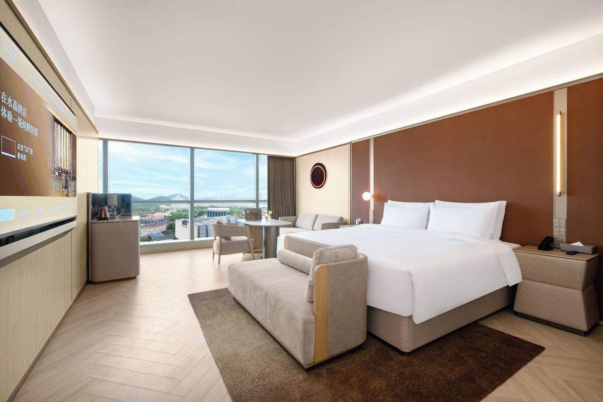 Quarto de hotel moderno com cama grande, escrivaninha, sofá e vista para a cidade.