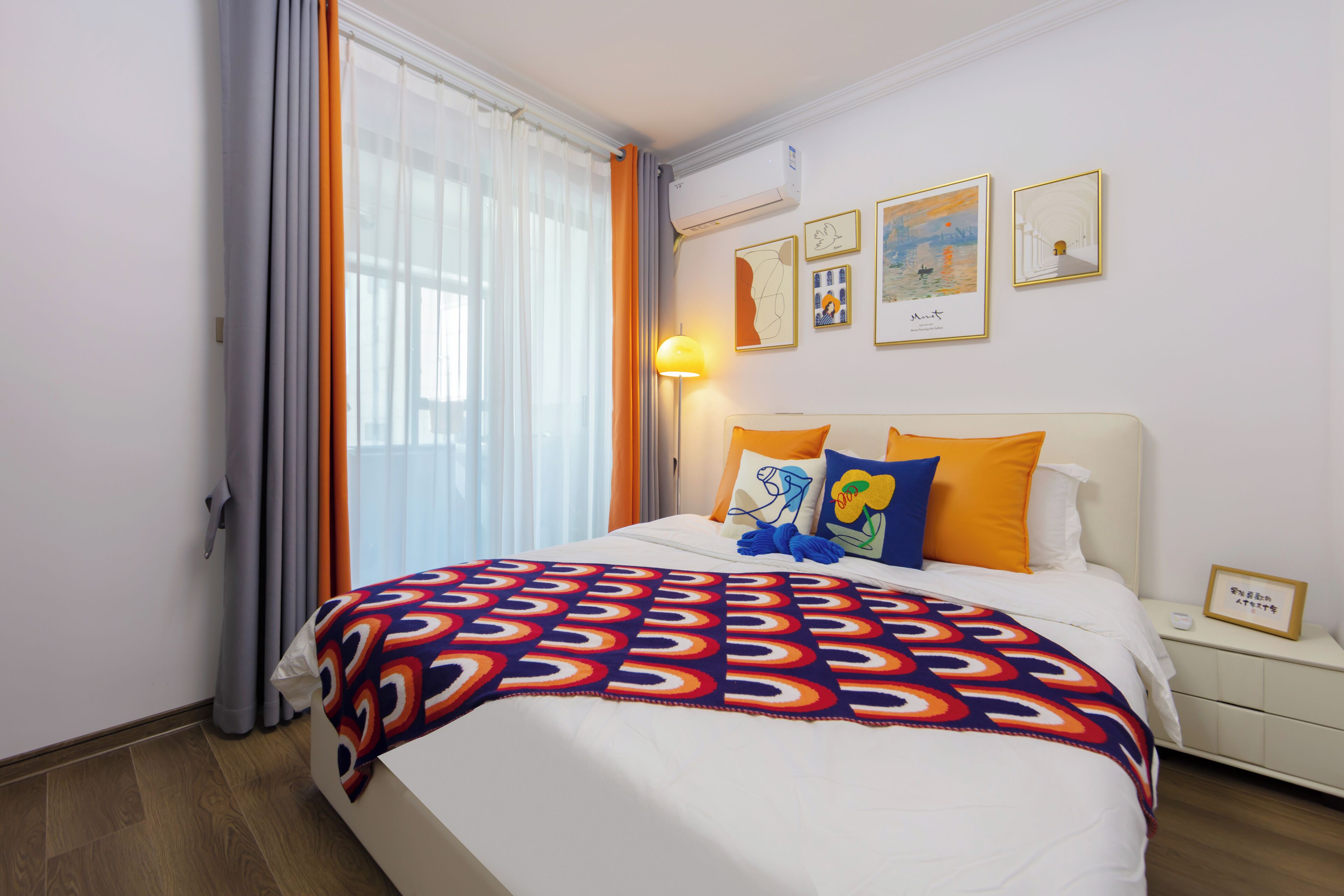 Quarto de hotel com cama, mesa de cabeceira, abajur e uma obra de arte na parede.