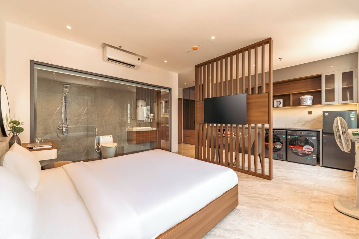 Quarto de hotel moderno com uma cama grande, chuveiro, televisão e uma cozinha compacta.