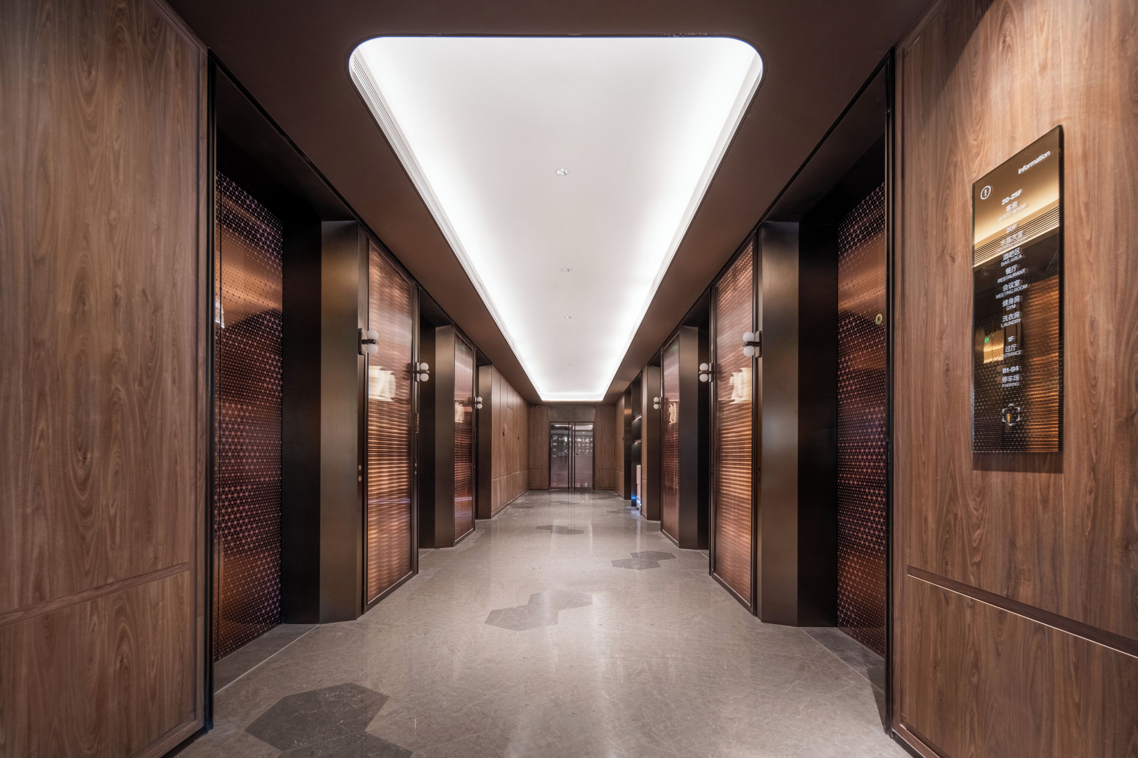 Um corredor moderno com lambris de madeira, luminária central e um diretório digital na parede.