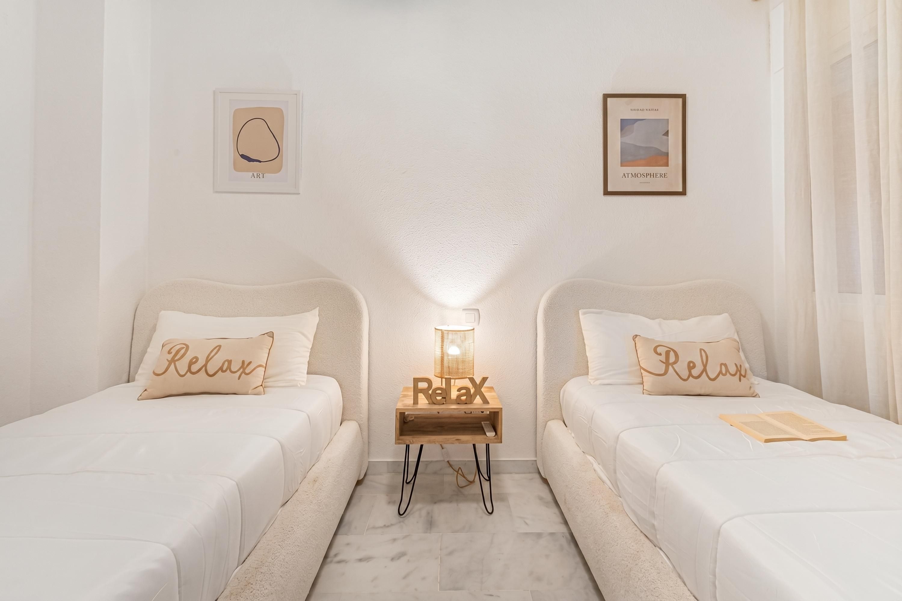 Quarto de hotel com duas camas, uma mesa de cabeceira com abajur e obras de arte nas paredes.