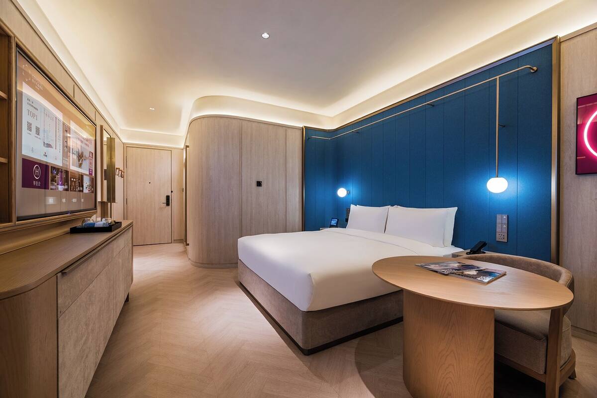 Quarto de hotel com cama, mesa de cabeceira e televisão fixada na parede.