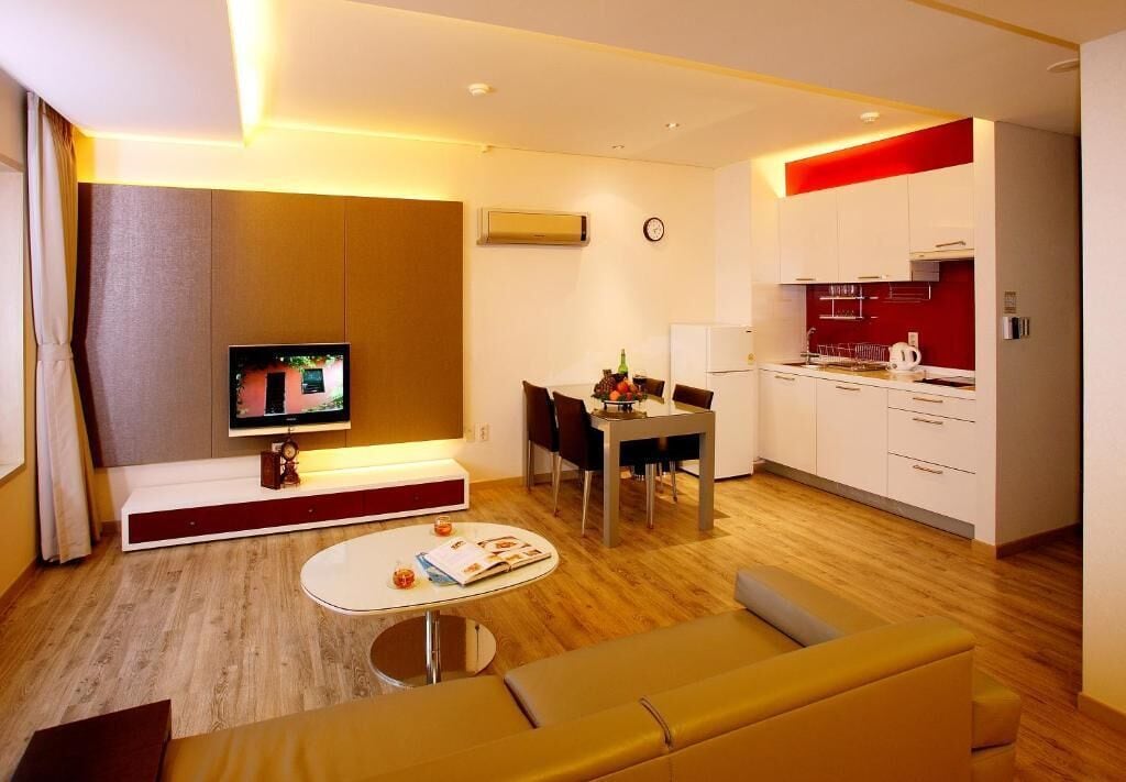 Uma sala de estar moderna com televisão de tela plana, área de jantar e cozinha com armários brancos.