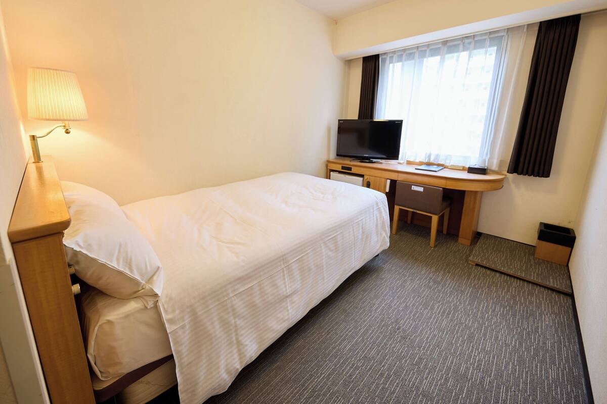 Quarto de hotel com cama, escrivaninha, cadeira, televisão e abajur.