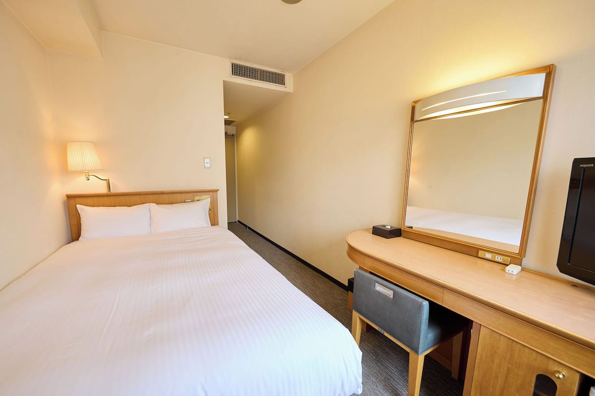 Quarto de hotel com cama, escrivaninha com espelho e abajur.