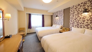 Quarto de hotel com duas camas, uma mesa, uma cadeira, janela com cortinas, parede com padrão floral e luminária no teto.